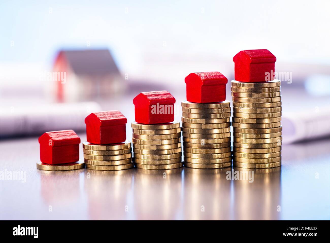Small red houses standing on stacks of coins with blueprints and ...