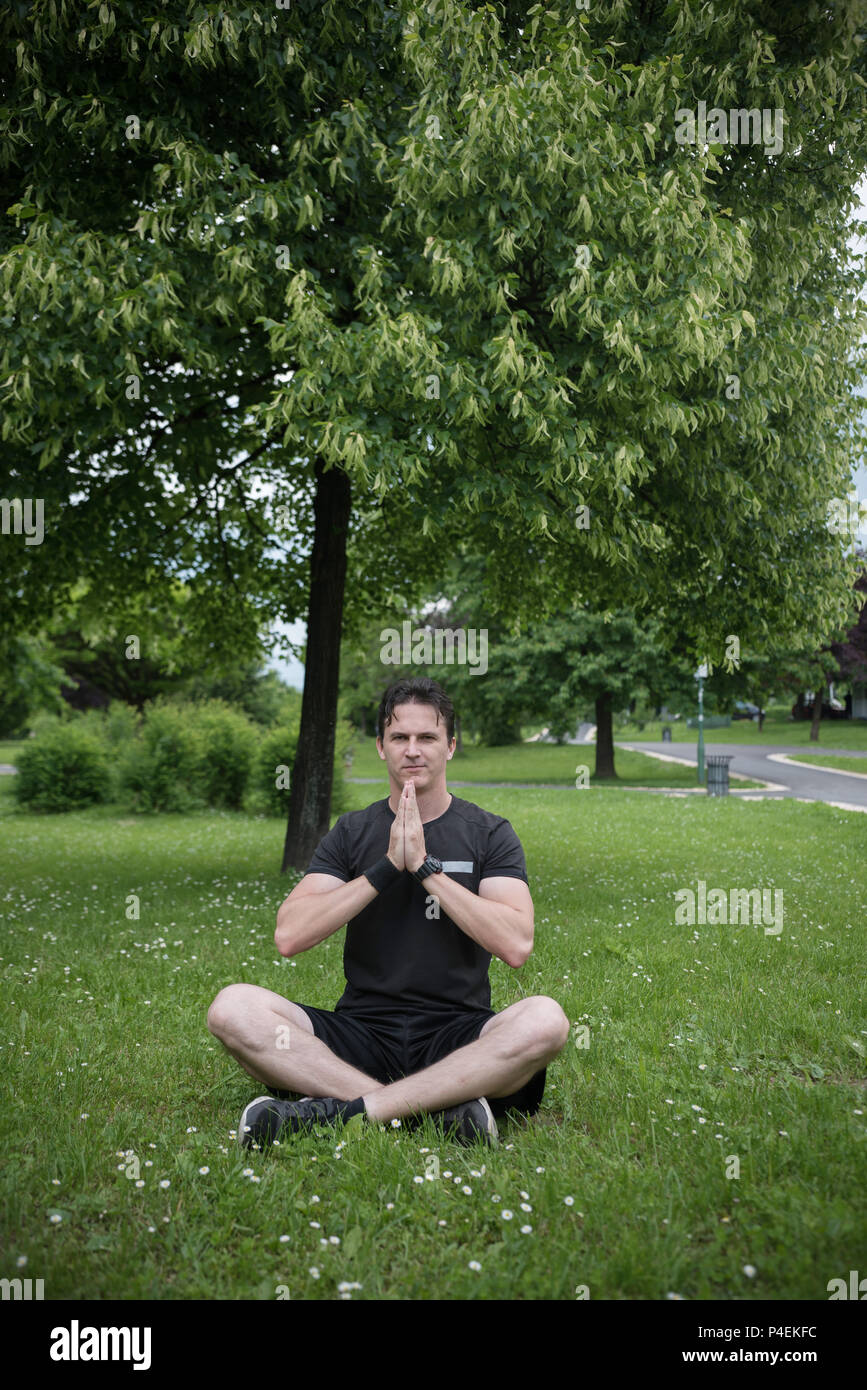 Man sitting cross-legged in a public park meditating Stock Photo - Alamy
