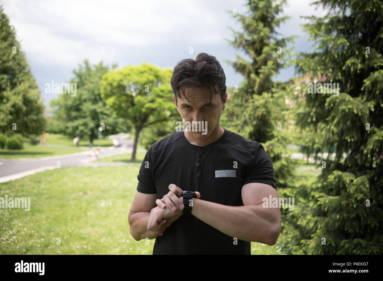 Man standing in park looking at his watch while exercising Stock Photo ...