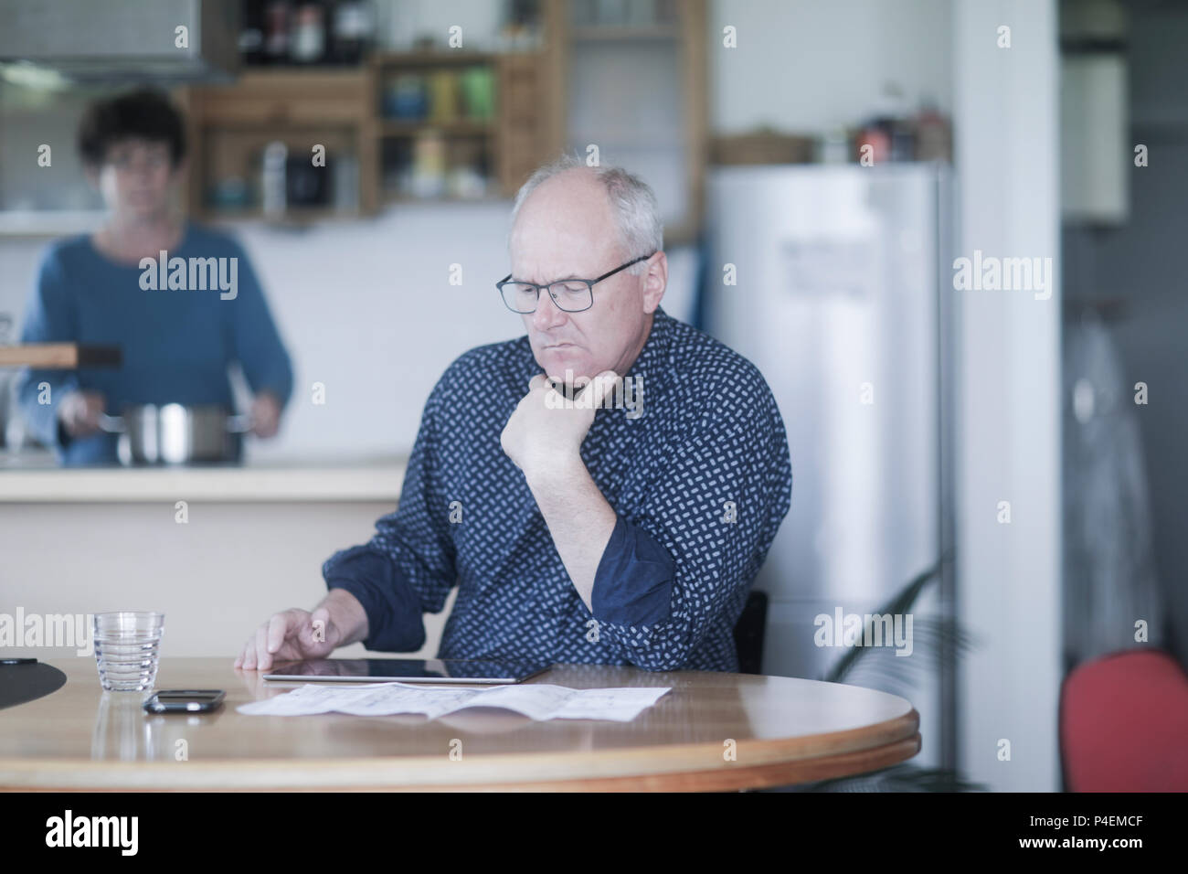 Man sitting at table working while his wife prepares food Stock Photo ...