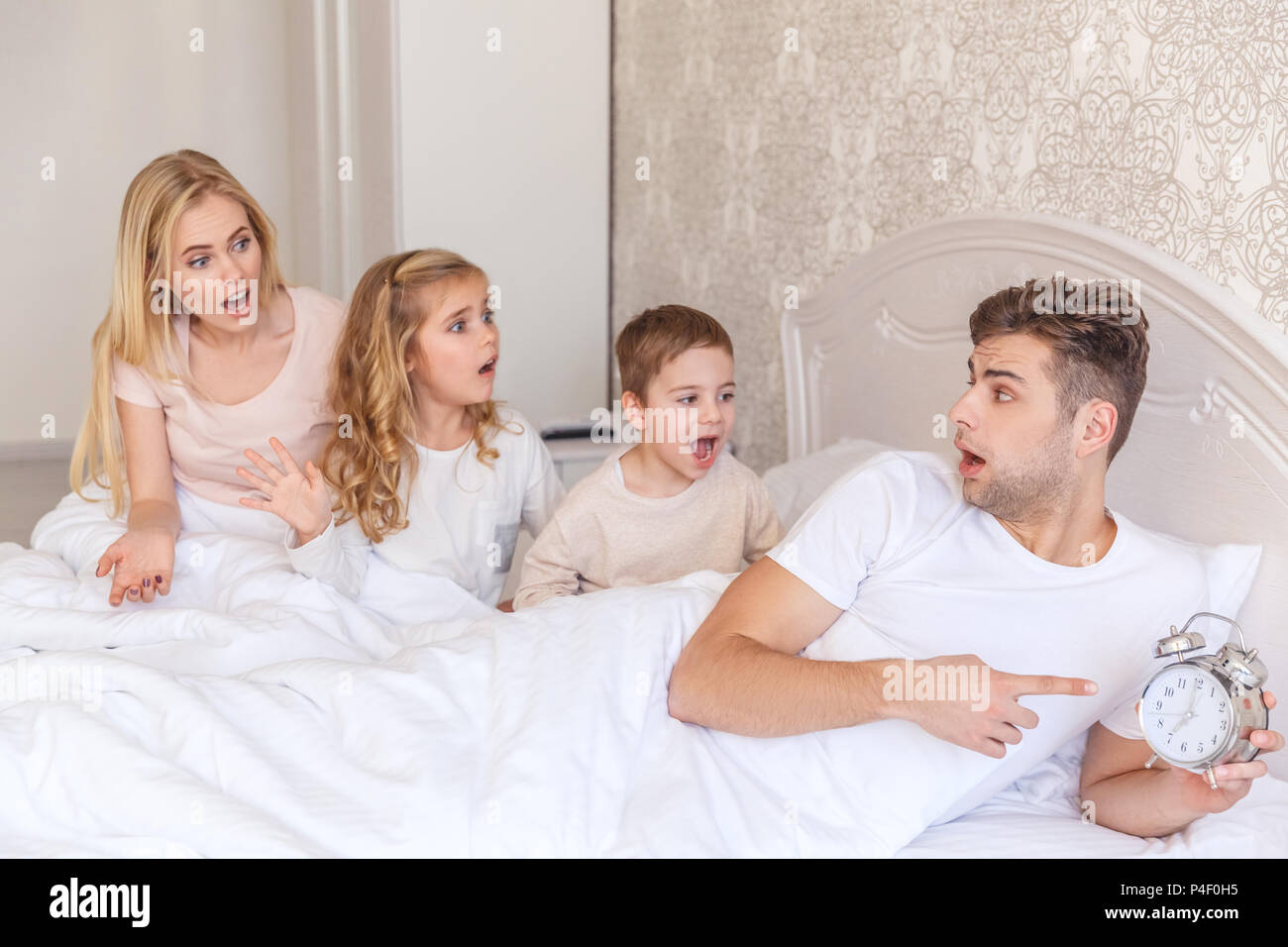 overslept young family in bed looking at alarm clock with shocked ...