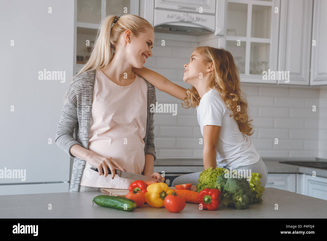 daughter hugging pregnant mother while she cooking at kitchen Stock ...
