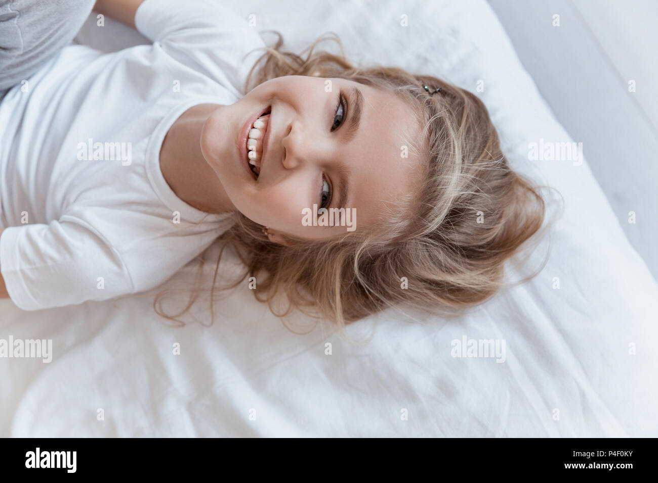 overhead view of smiling kid lying on bed on back and looking away ...