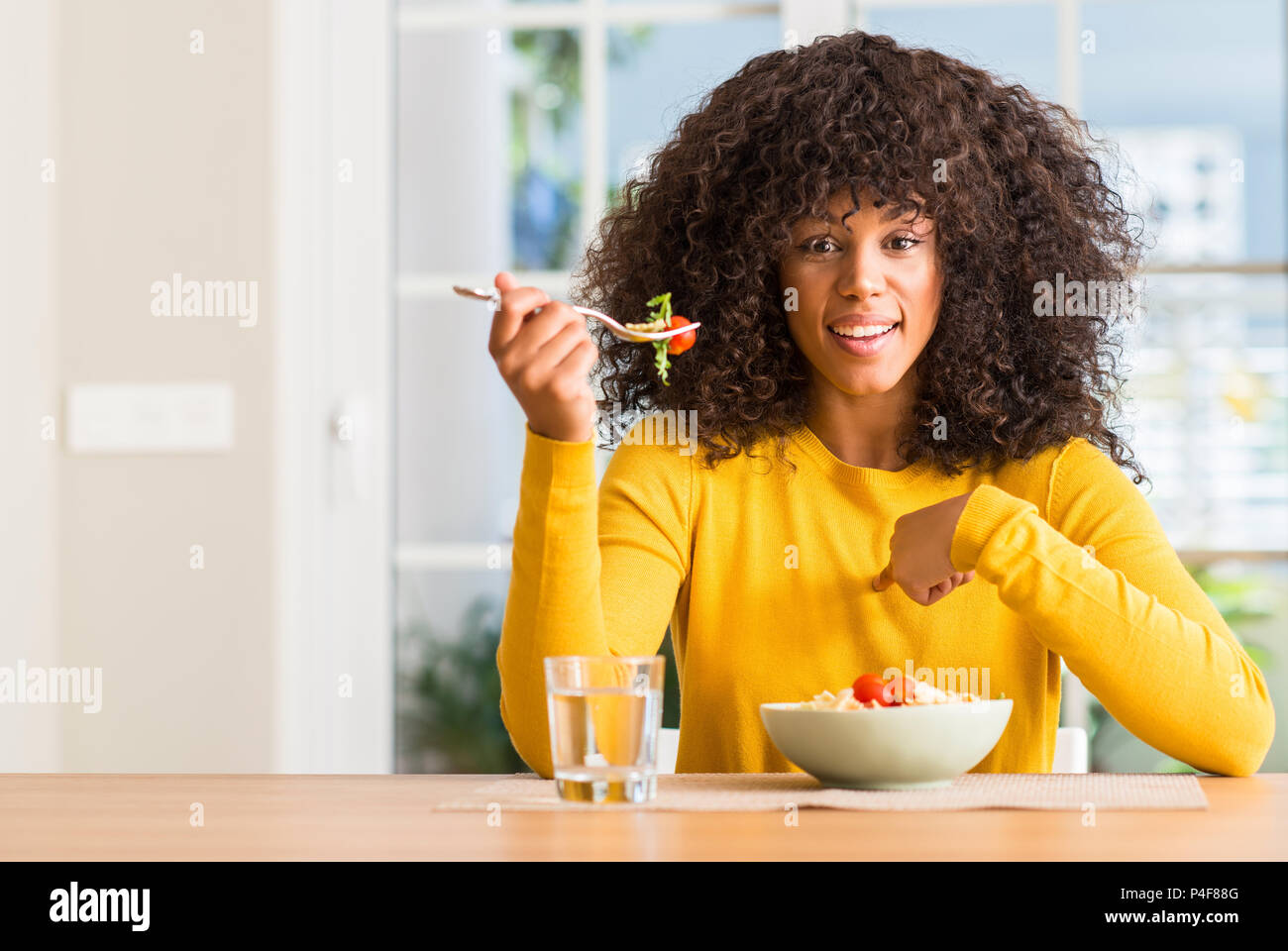 African american woman eating pasta salad at home with surprise face ...