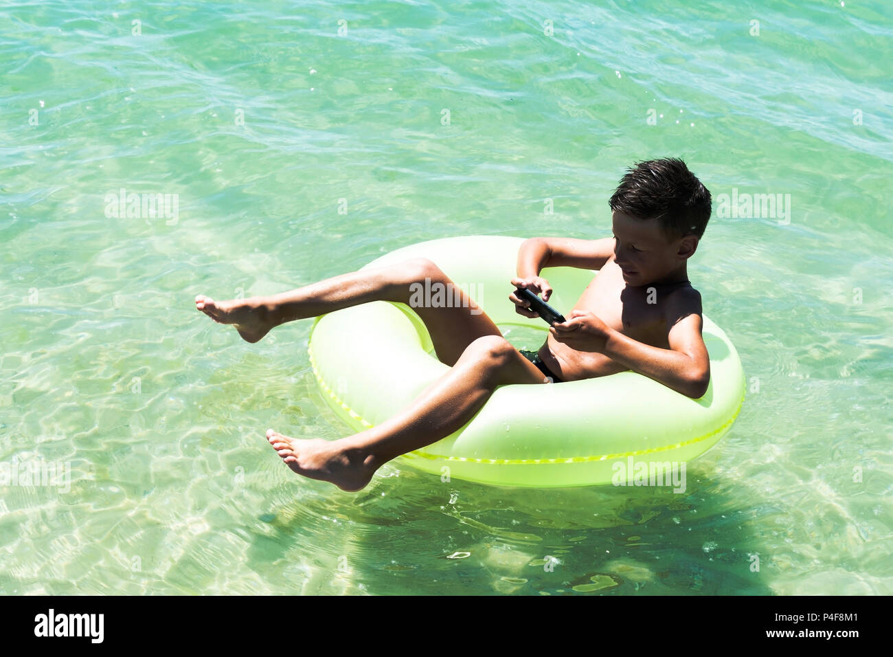 Boy swimming in inflatable ring with smart phone Stock Photo - Alamy