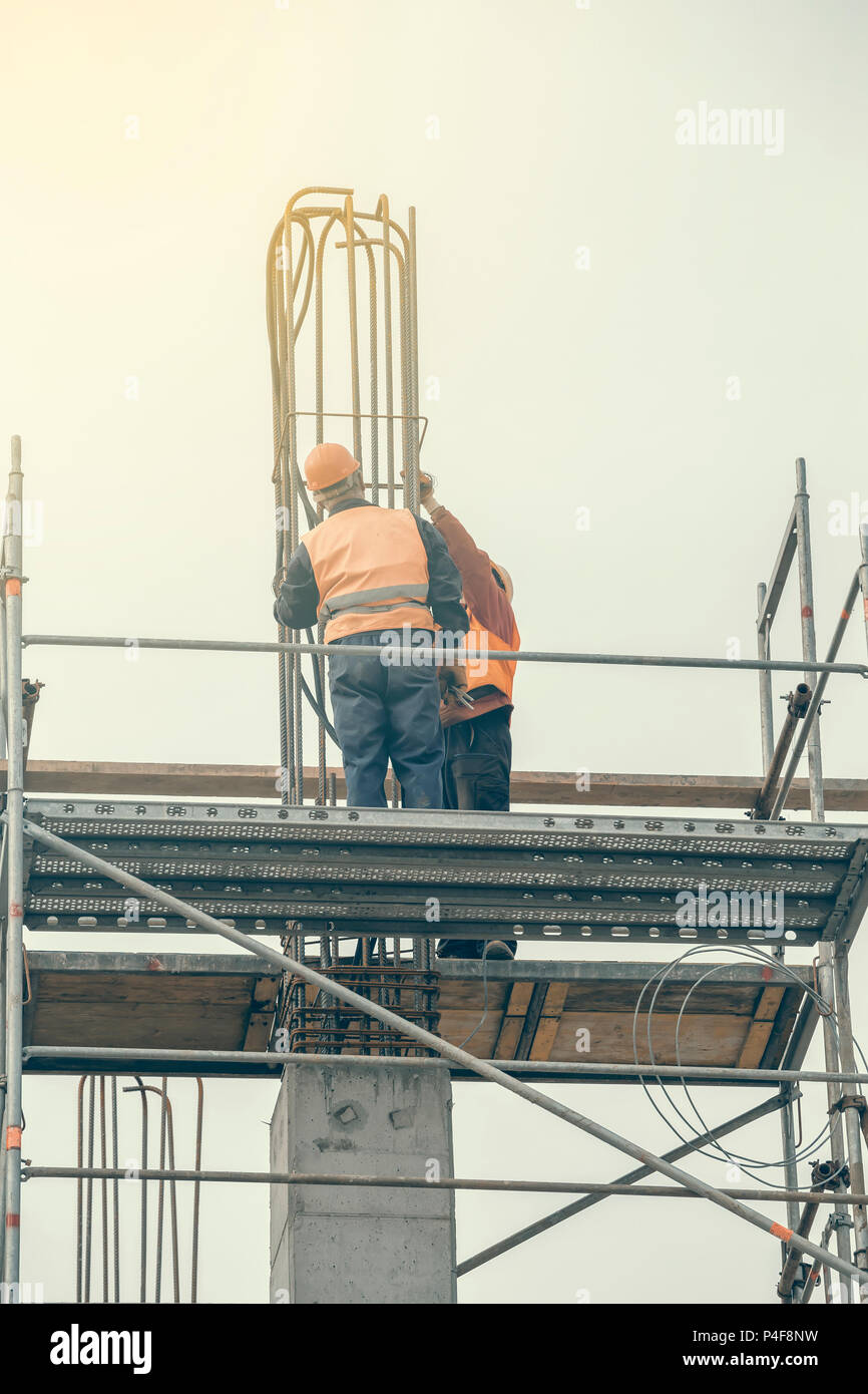 Workers on scaffold platform tied rebar and steel bars, concrete pillar ...