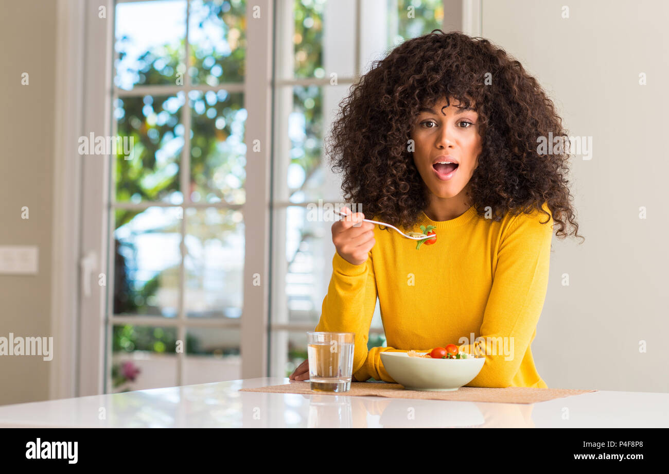 African american woman eating pasta salad scared in shock with a ...
