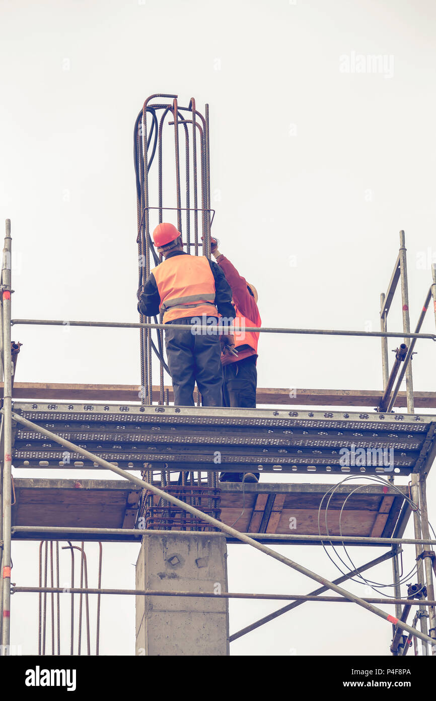 Workers on scaffold platform tied rebar and steel bars, concrete pillar ...