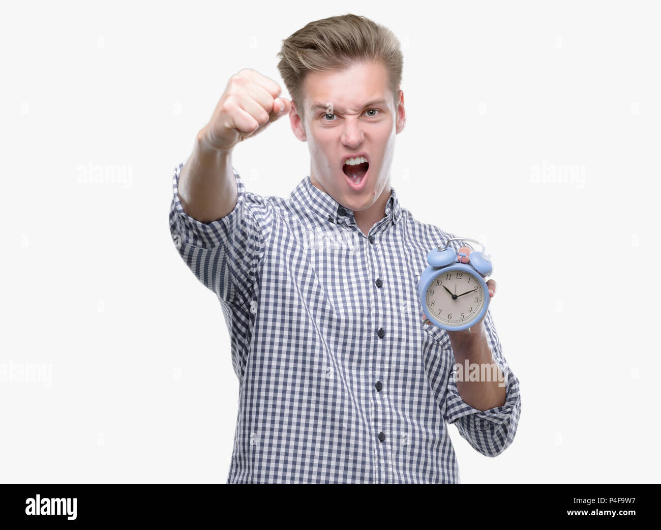 Young handsome blond man holding alarm clock annoyed and frustrated ...