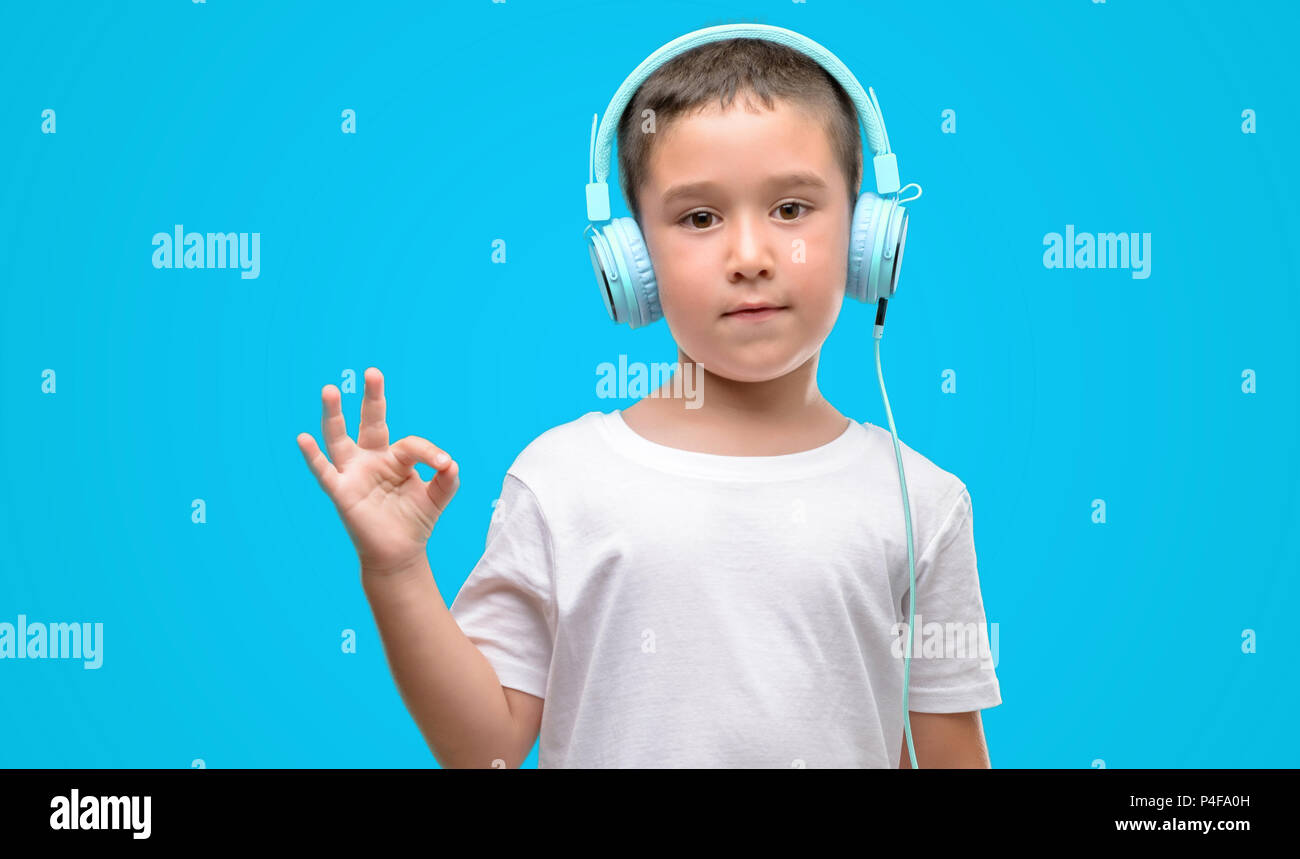 Dark haired little child listening music with headphones doing ok sign ...
