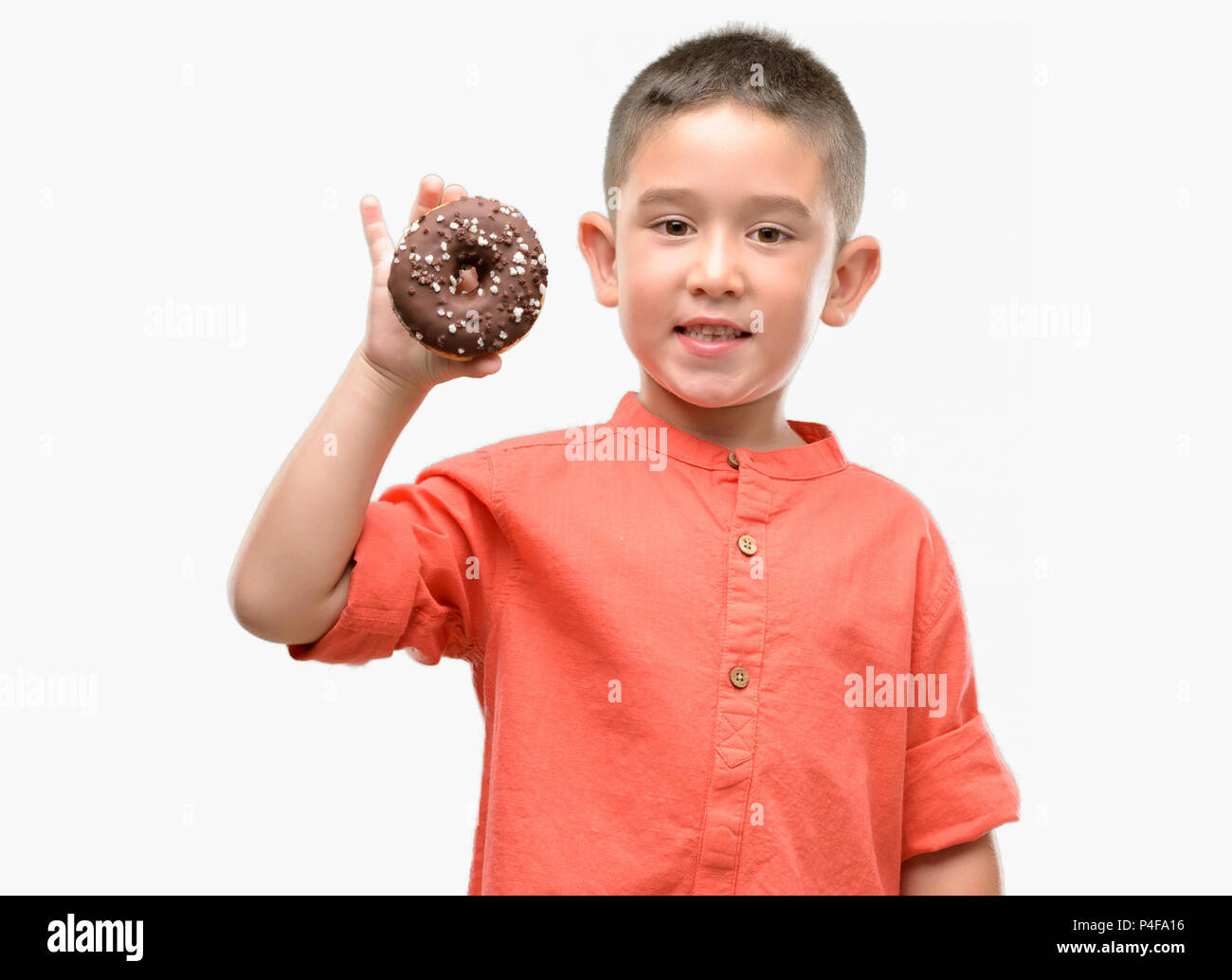 Dark haired little child eating doughnut with a happy face standing and ...