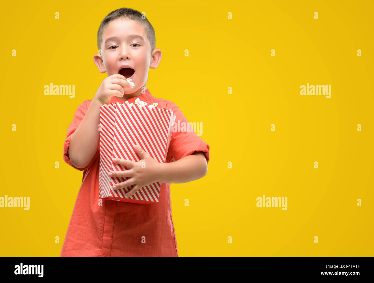 Dark haired little child eating popcorn with a happy face standing and ...