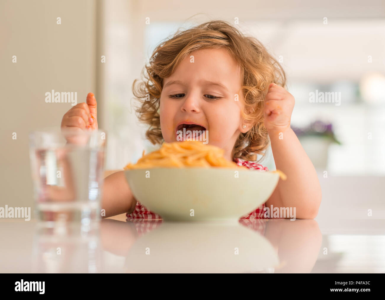 Beautiful blond child eating spaghetti with hands crying with tantrum ...