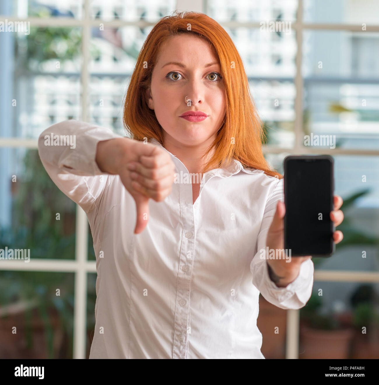 Redhead woman using smartphone at home with angry face, negative sign ...