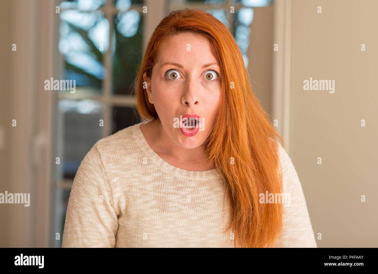Redhead woman at home scared in shock with a surprise face, afraid and ...