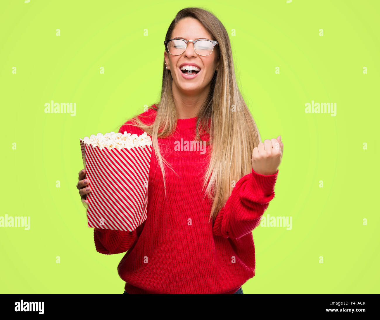 Beautiful young woman eating popcorn screaming proud and celebrating ...