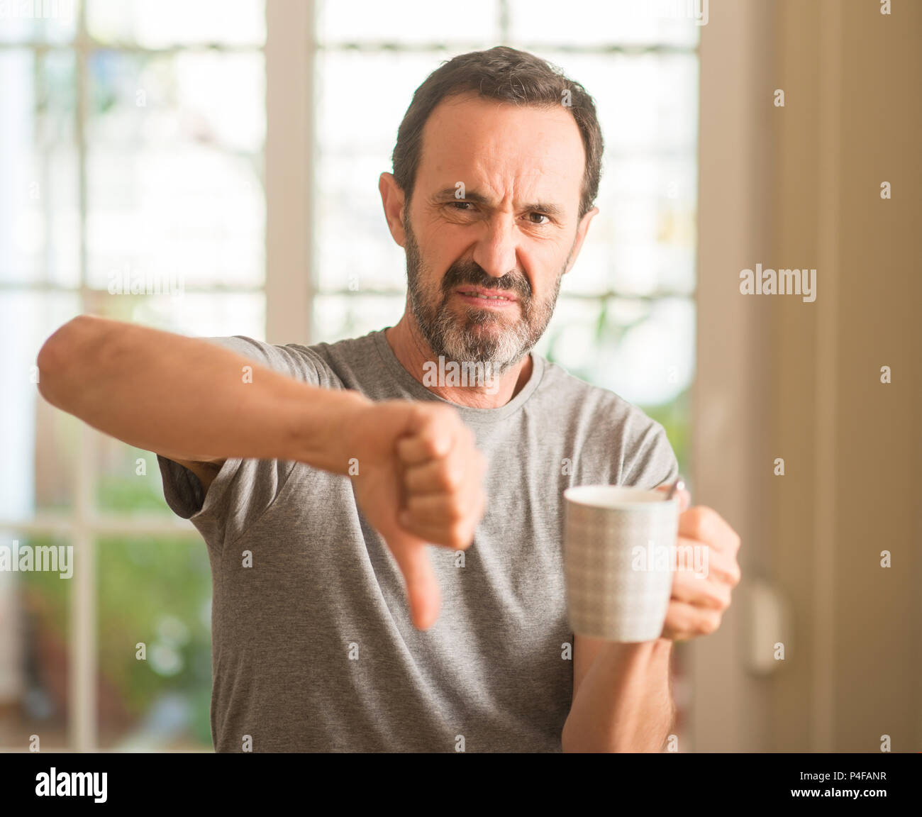 Middle age man drinking coffee in a cup with angry face, negative sign ...