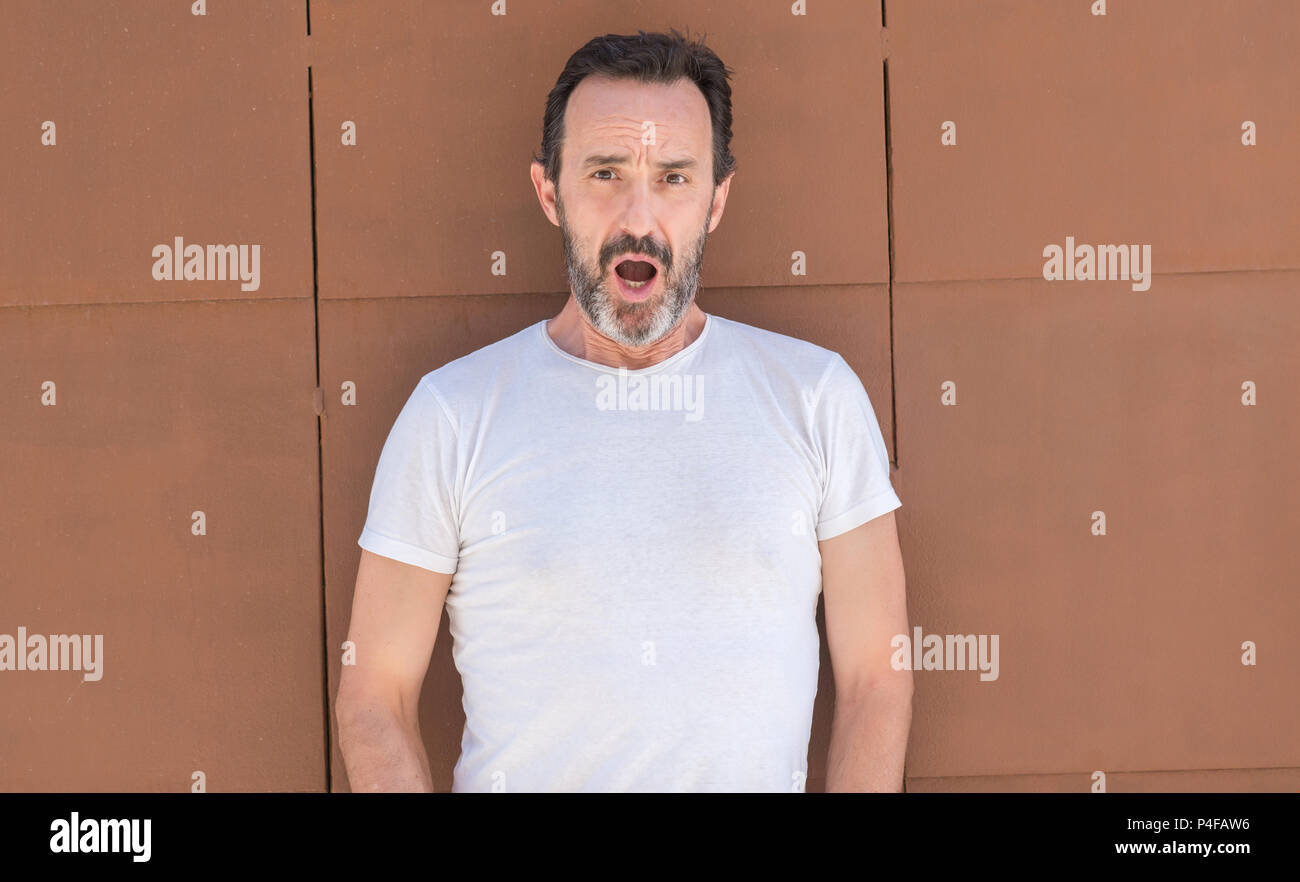 Handsome senior man standing over wall scared in shock with a surprise ...