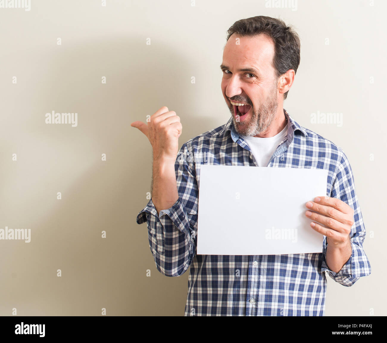 Senior man holding blank paper sheet pointing with hand and finger up ...
