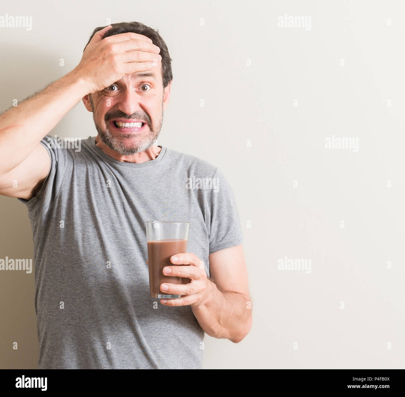 Senior man drinking chocolate milk shake stressed with hand on head ...