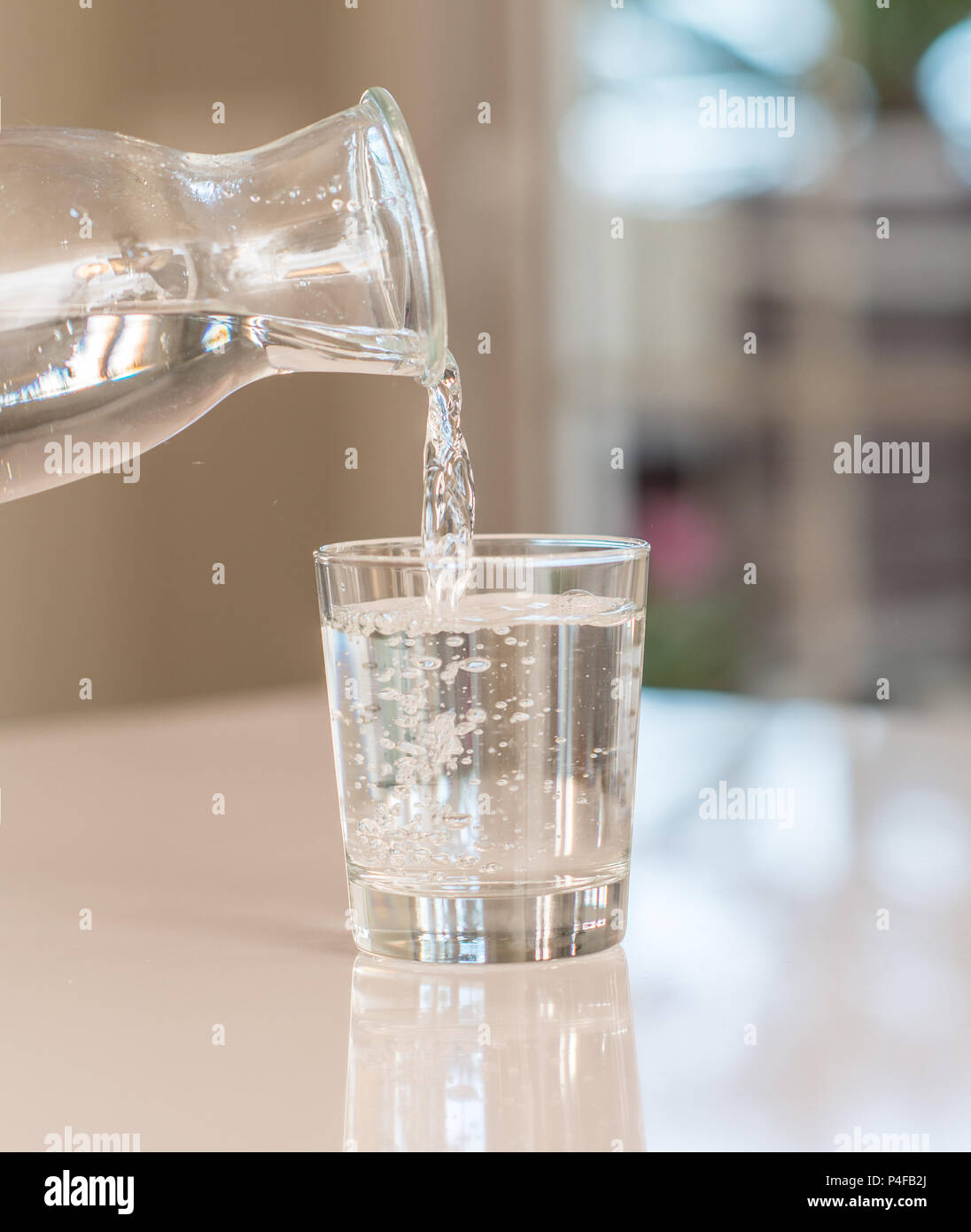 Closeup of bottle pouring water in a glass on the table with sunny bokeh background at home ...