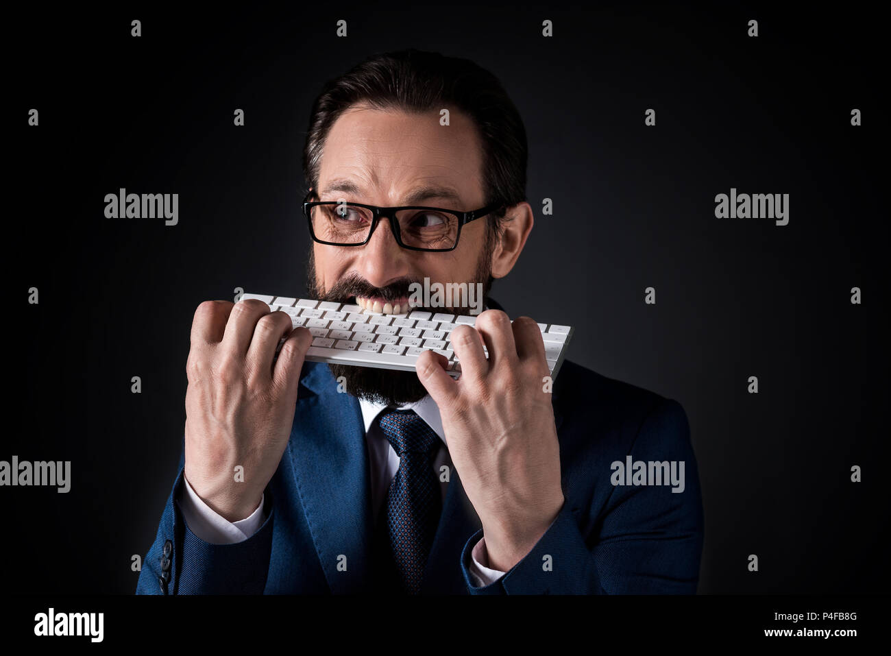 nervous bearded mature businessman biting keyboard isolated on black ...