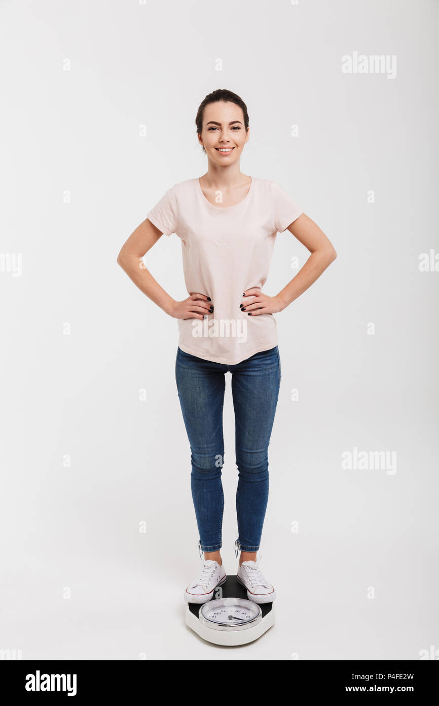 young woman standing on scales with arms akimbo isolated on white Stock ...