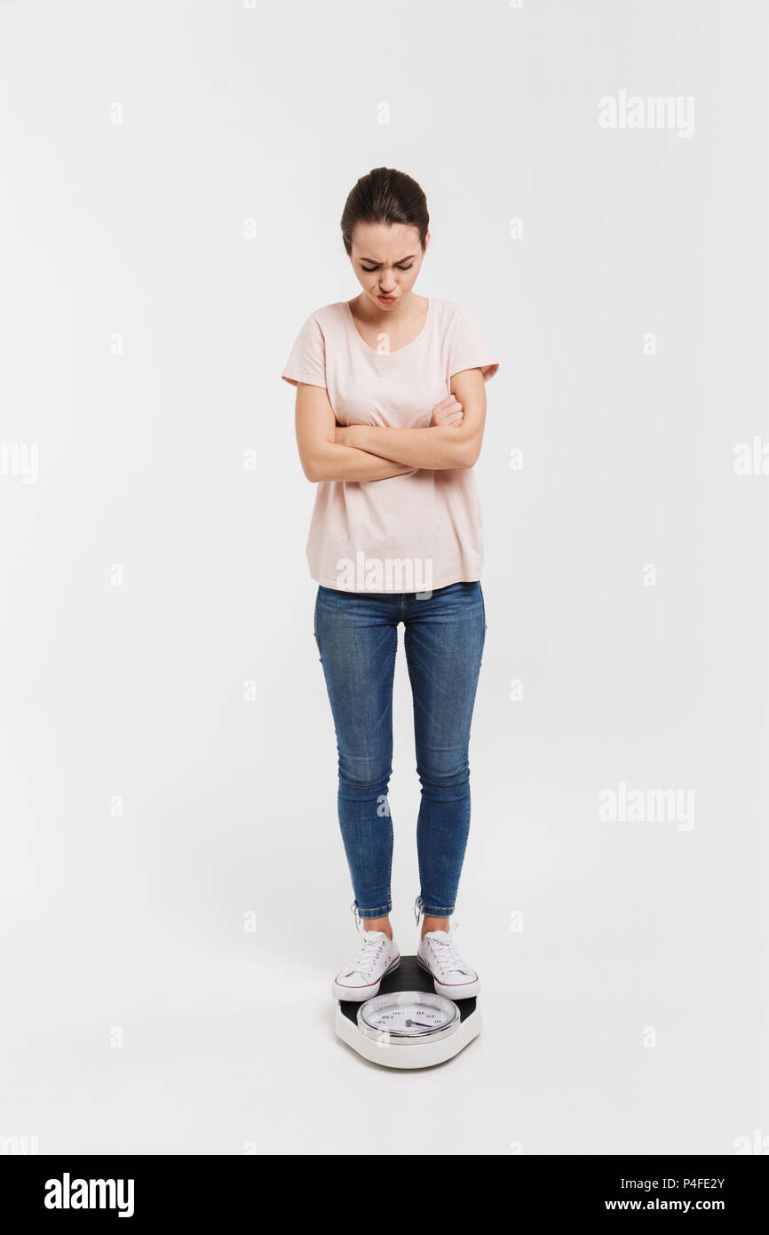 disappointed young woman standing on scales with crossed arms isolated ...