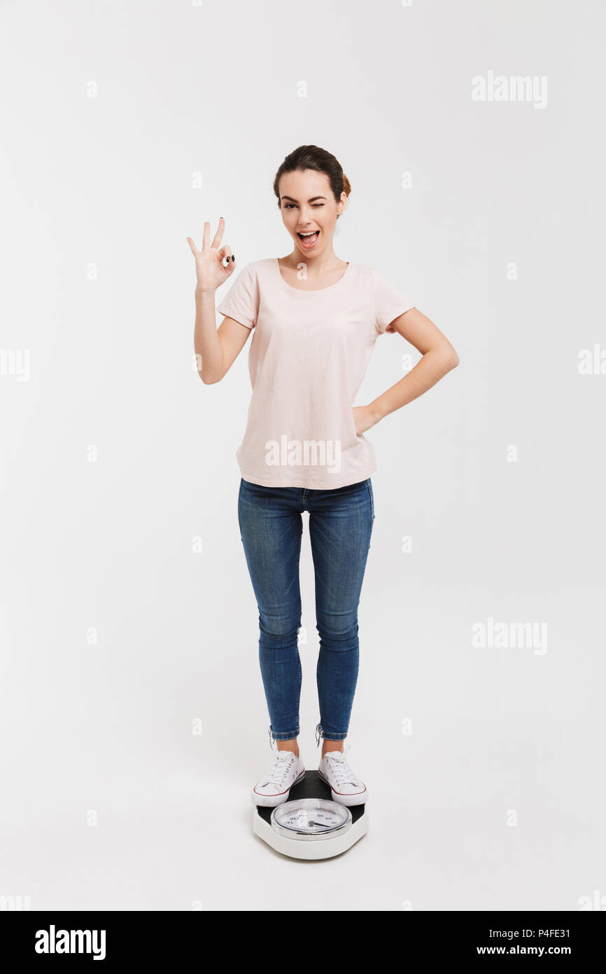 young woman showing okay sign while standing on scales isolated on ...