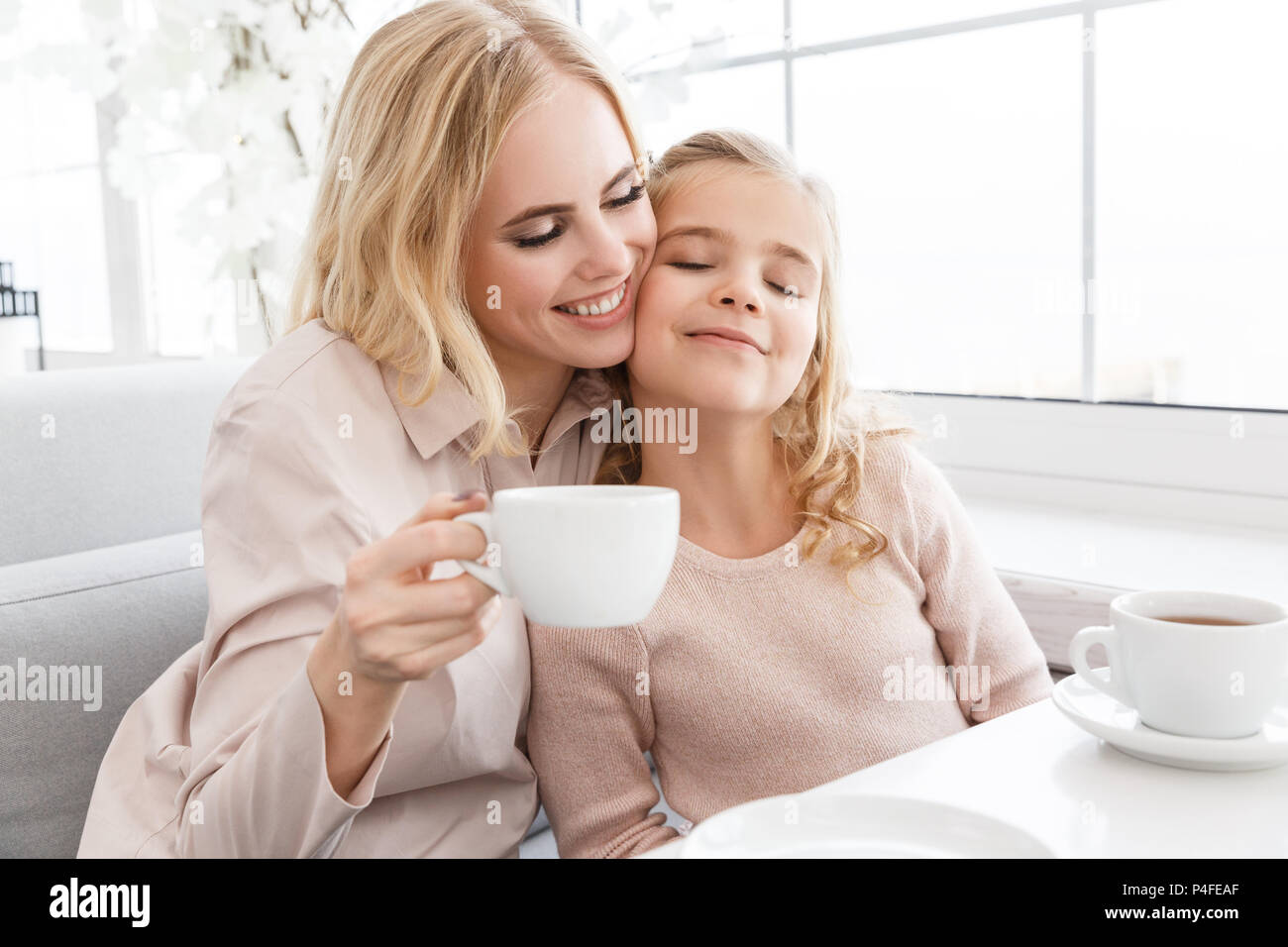 mother and daughter cuddling while drinking tea in cafe Stock Photo - Alamy