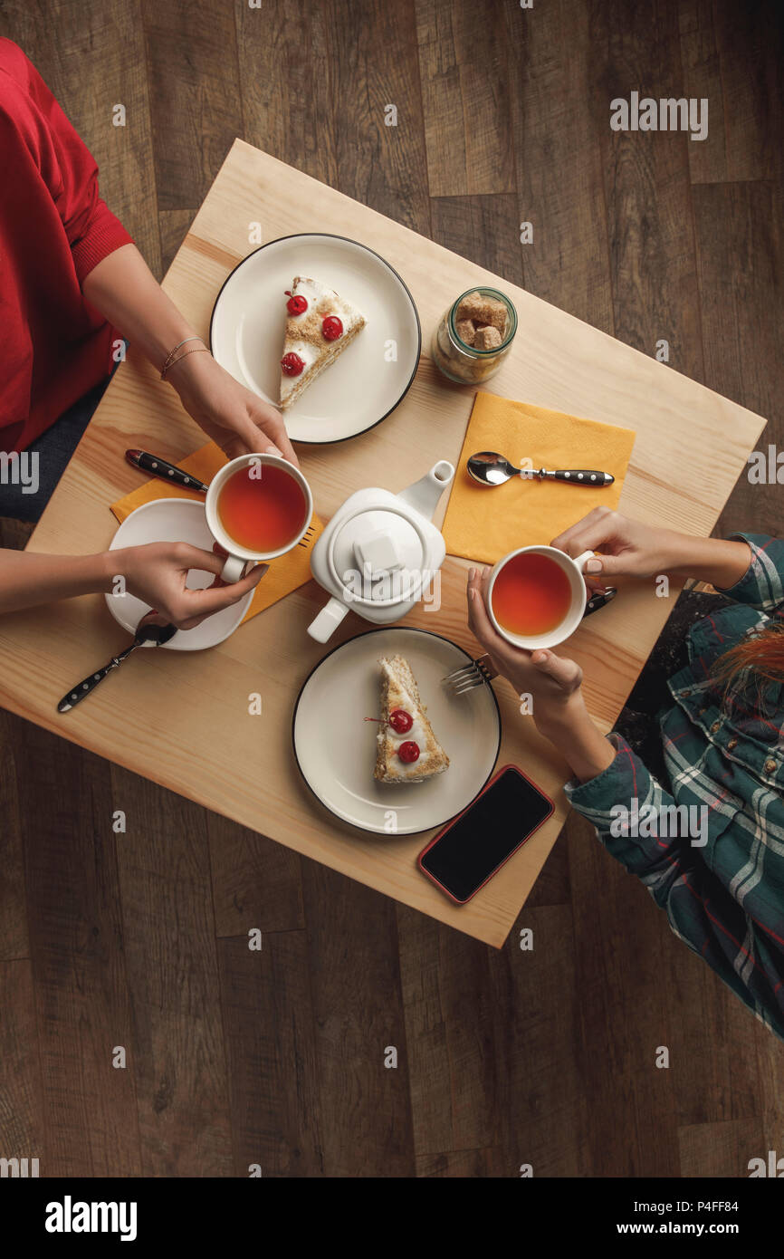 top view of two people drinking tea above table with pastries and ...