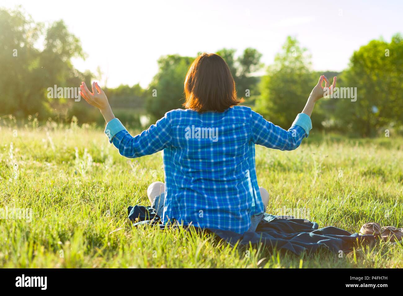Woman meditating, practicing yoga in nature, view from the back. Sunset ...