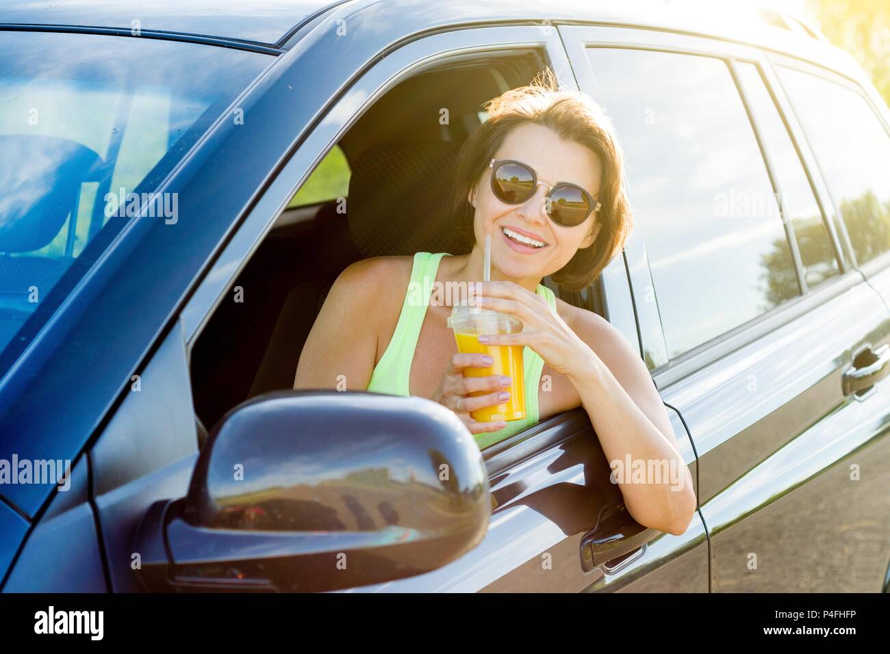 Beautiful female driver smiling while driving his car, drinking orange ...