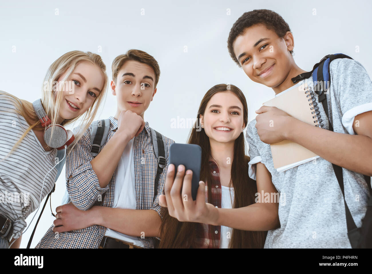 low angle view of multicultural smiling teenagers using smartphone ...