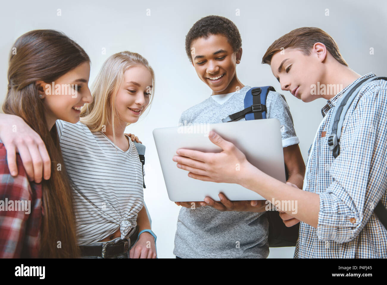 multiethnic group of smiling teenagers using laptop together isolated ...