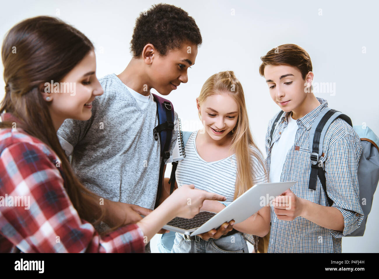 multiethnic group of smiling teenagers using laptop together isolated ...