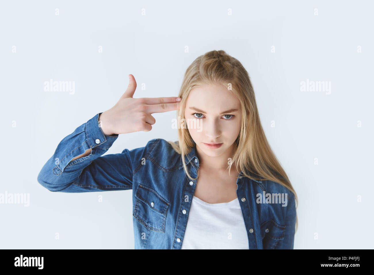 portrait of teen girl aiming hand to head and looking at camera ...