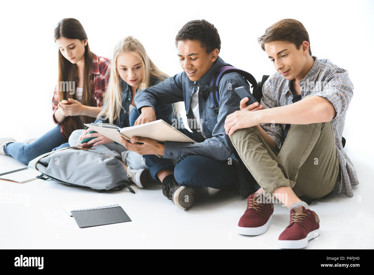 multiethnic students doing homework while friends using smartphones ...