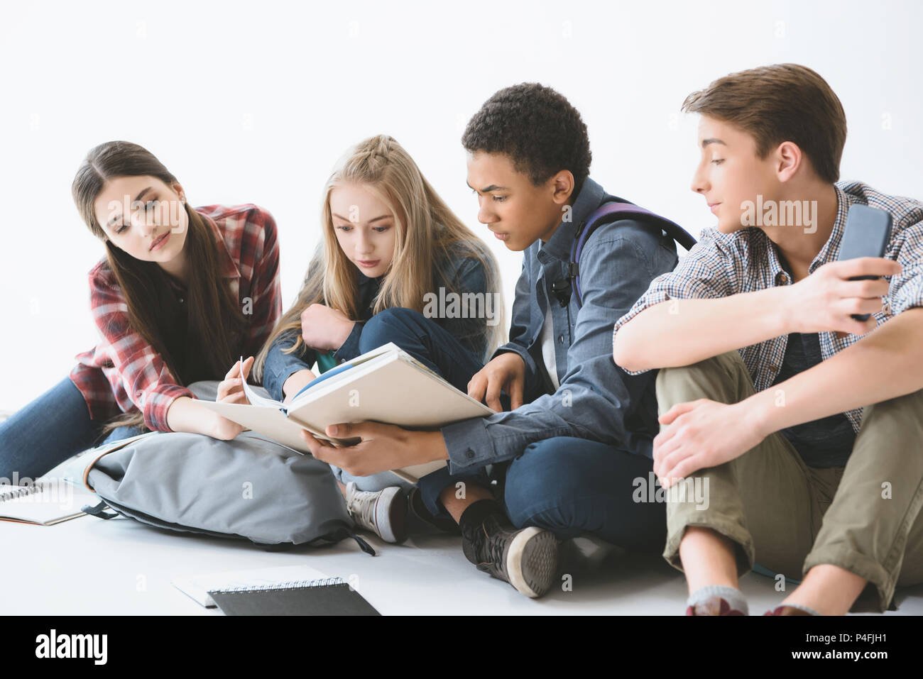 multiethnic students doing homework while friend using smartphone near ...