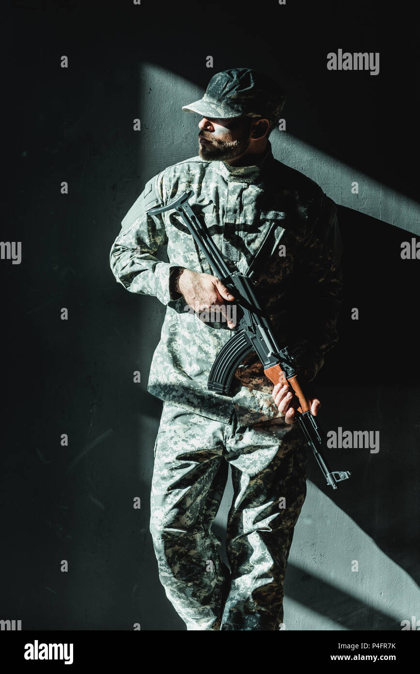 soldier in military uniform with rifle leaning back on concrete wall ...