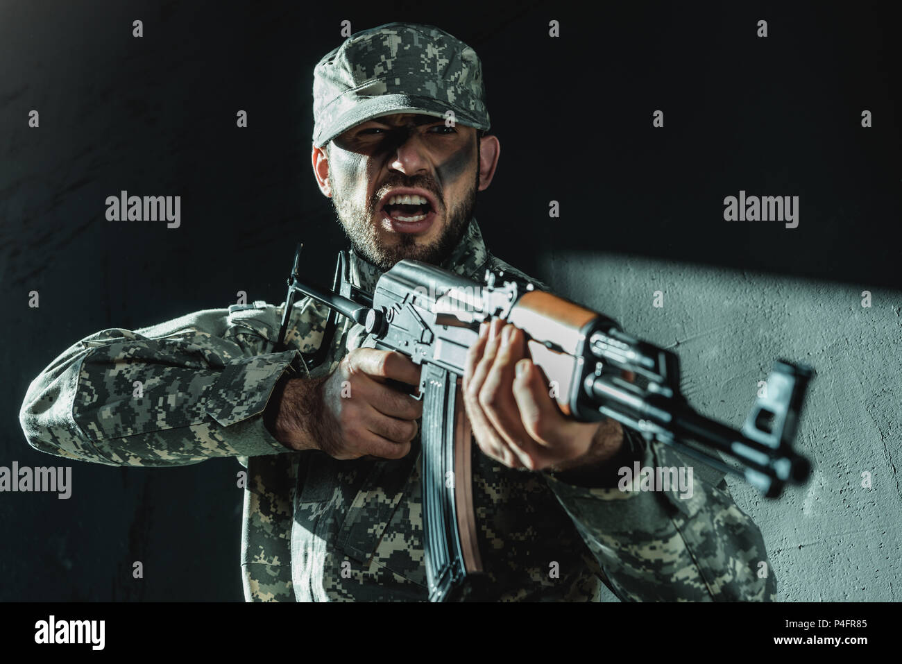 shouting soldier in military uniform with rifle next to concrete wall ...