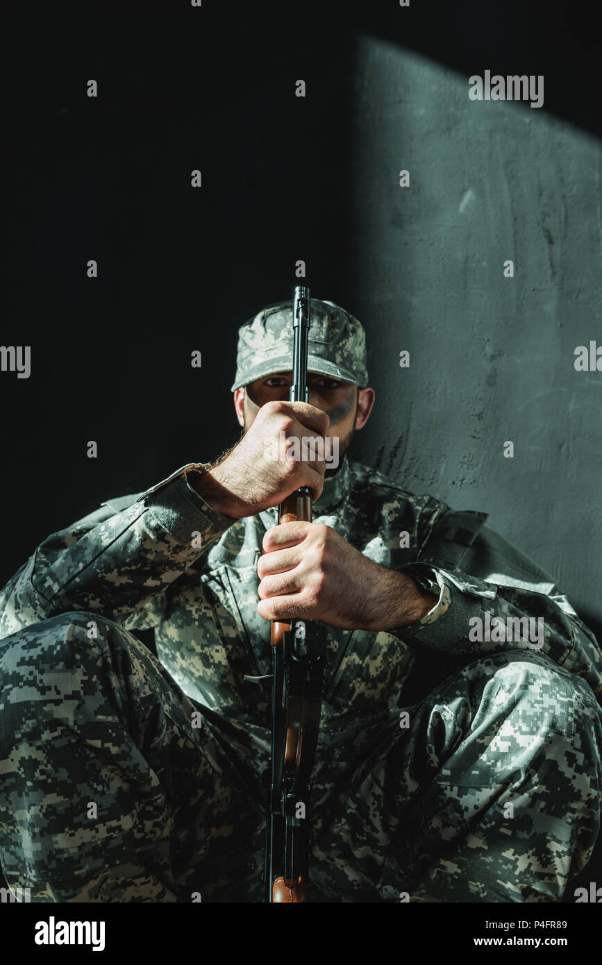 soldier in military uniform with rifle sitting next to concrete wall ...