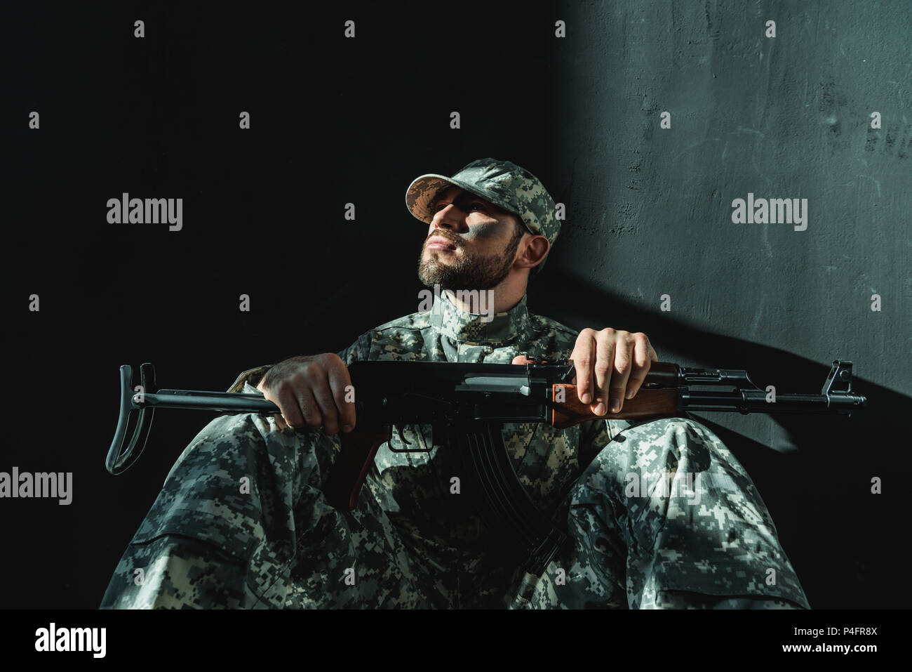 soldier in military uniform with rifle sitting next to concrete wall ...