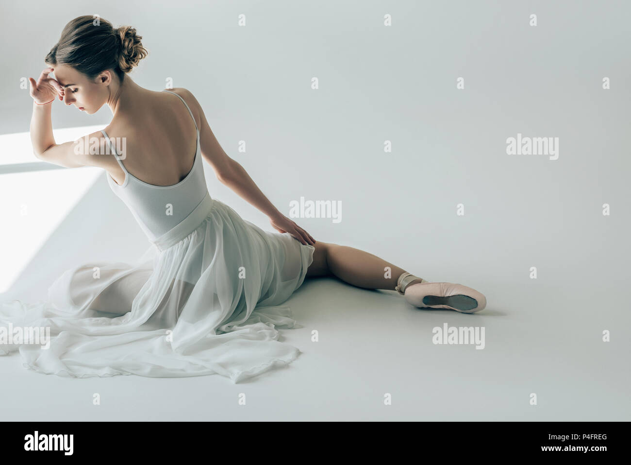 back view of elegant ballerina sitting in white dress and ballet shoes ...