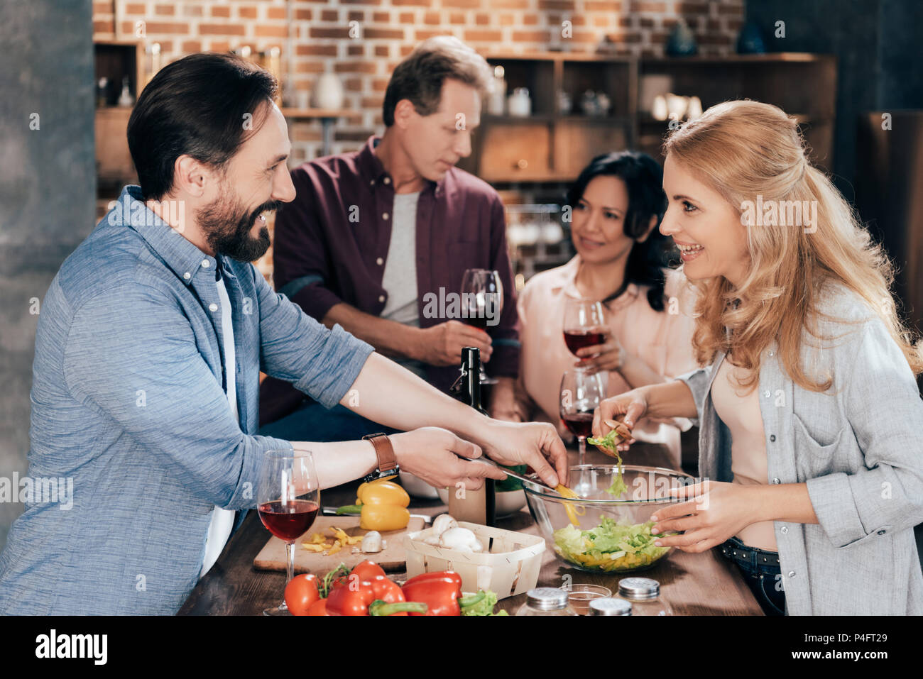 cheerful mature friends drinking wine while cooking dinner together ...