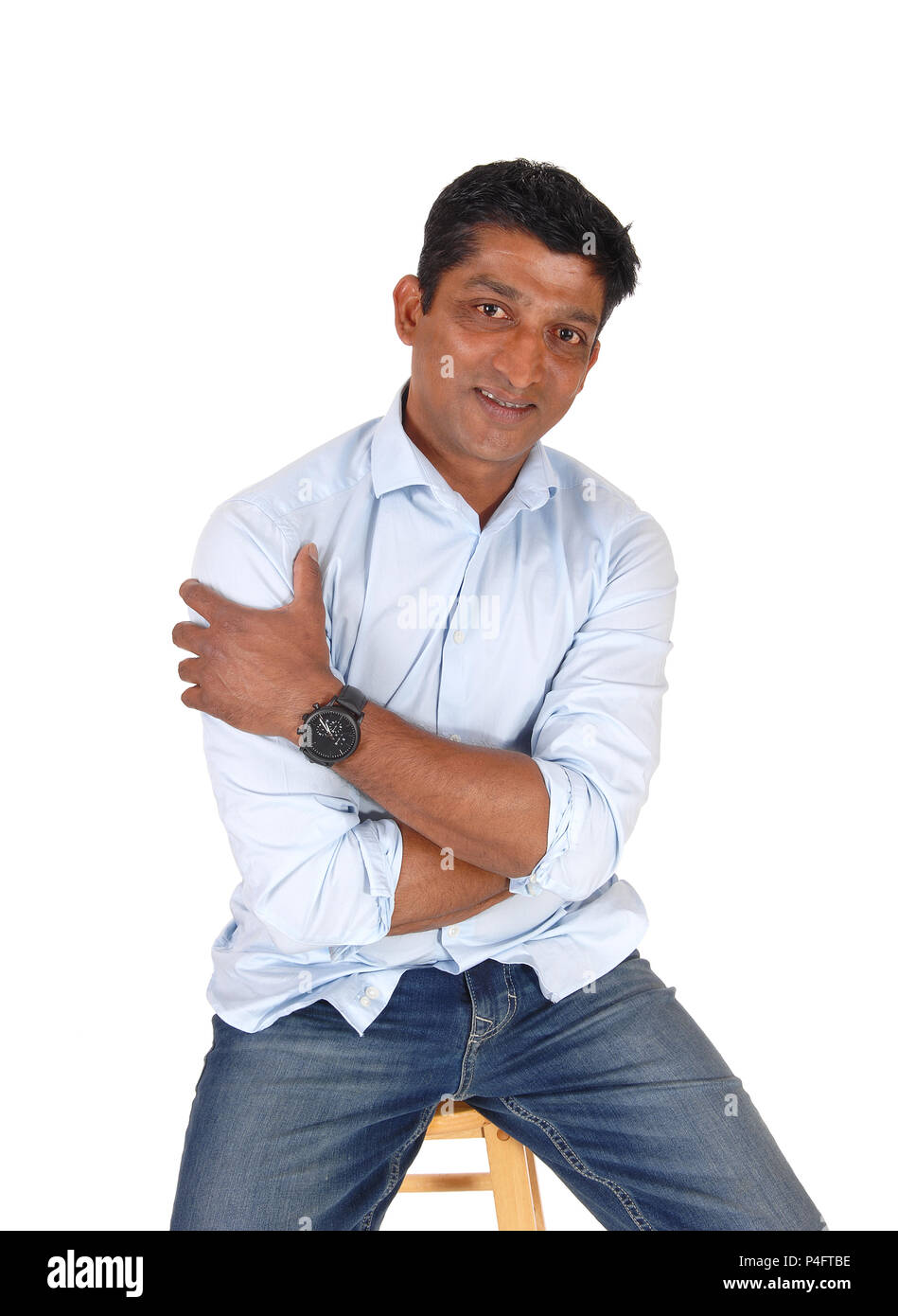 A handsome middle age East Indian man sitting on a bar chair in jeans ...