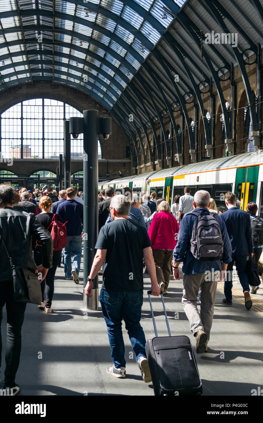 Commuters walk along a platform towards the exit with trains alongside ...