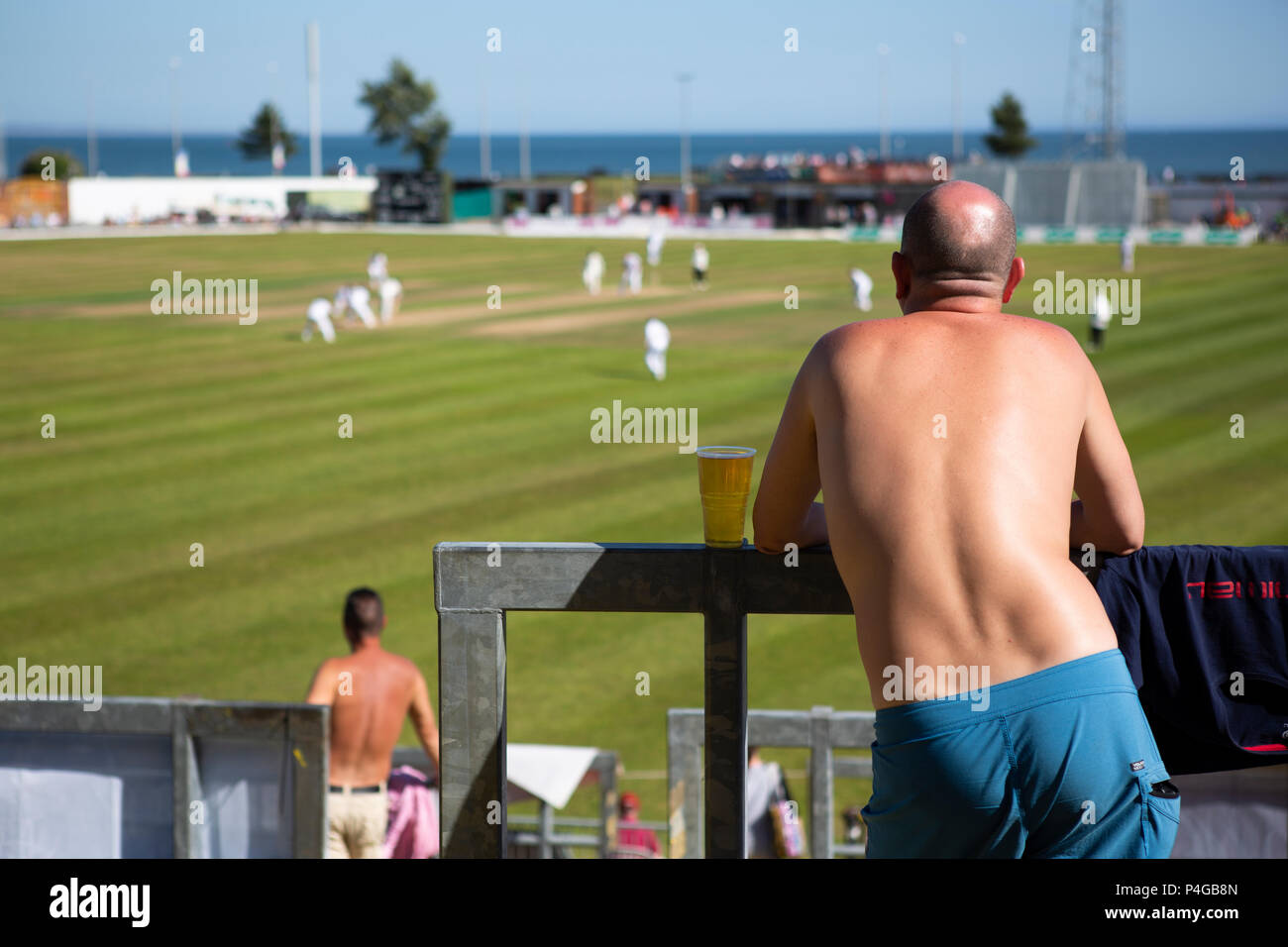 A topless spectator enjoys a cold beer on a hot day watching cricket in ...