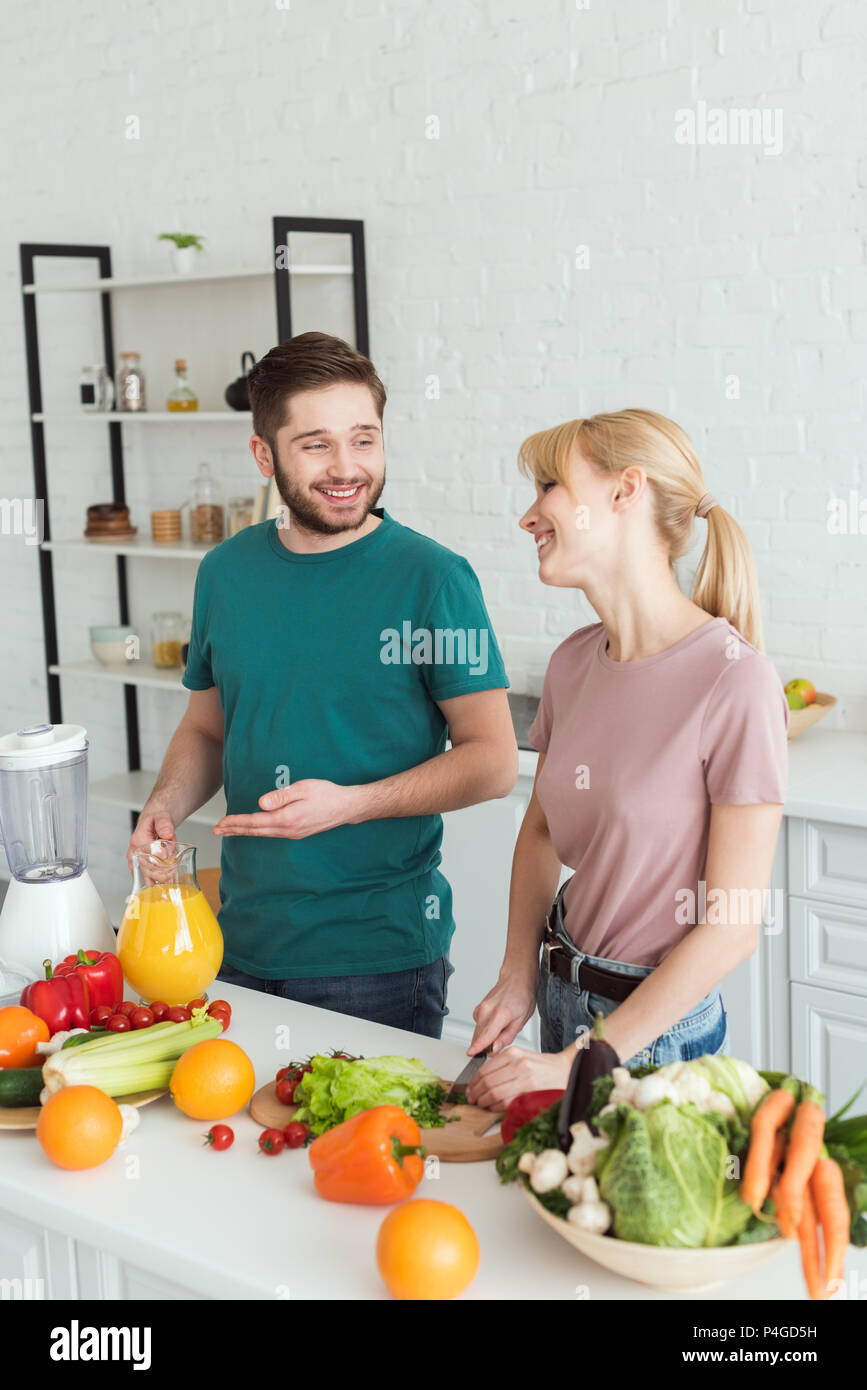 couple of vegans smiling and talking while cooking food at kitchen ...
