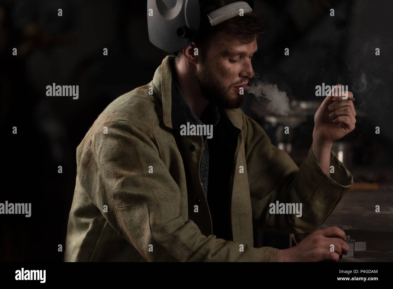 workman with lifted up protective mask sitting and smoking cigarette at ...